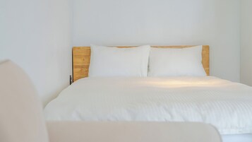 Uma cama com roupa de cama branca e cabeceira de madeira em um quarto com paredes brancas.