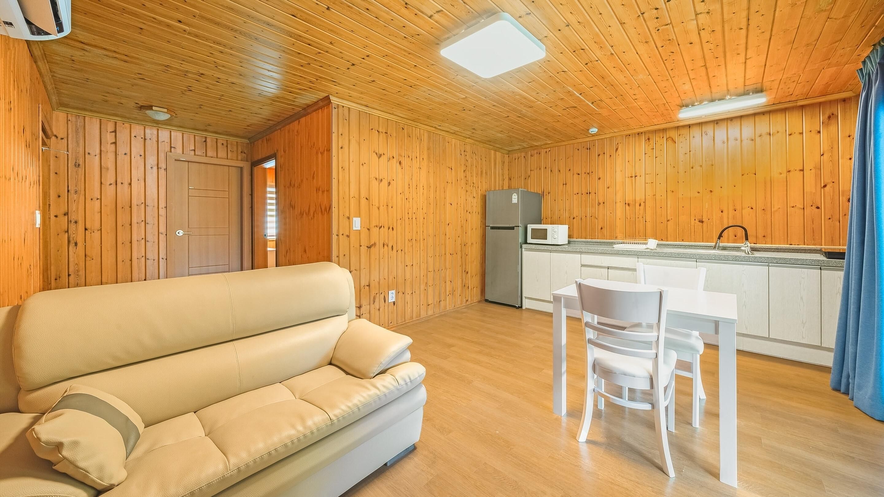 Um quarto aconchegante com sofá e mesa de jantar com cadeiras, paredes de madeira e cozinha compacta.