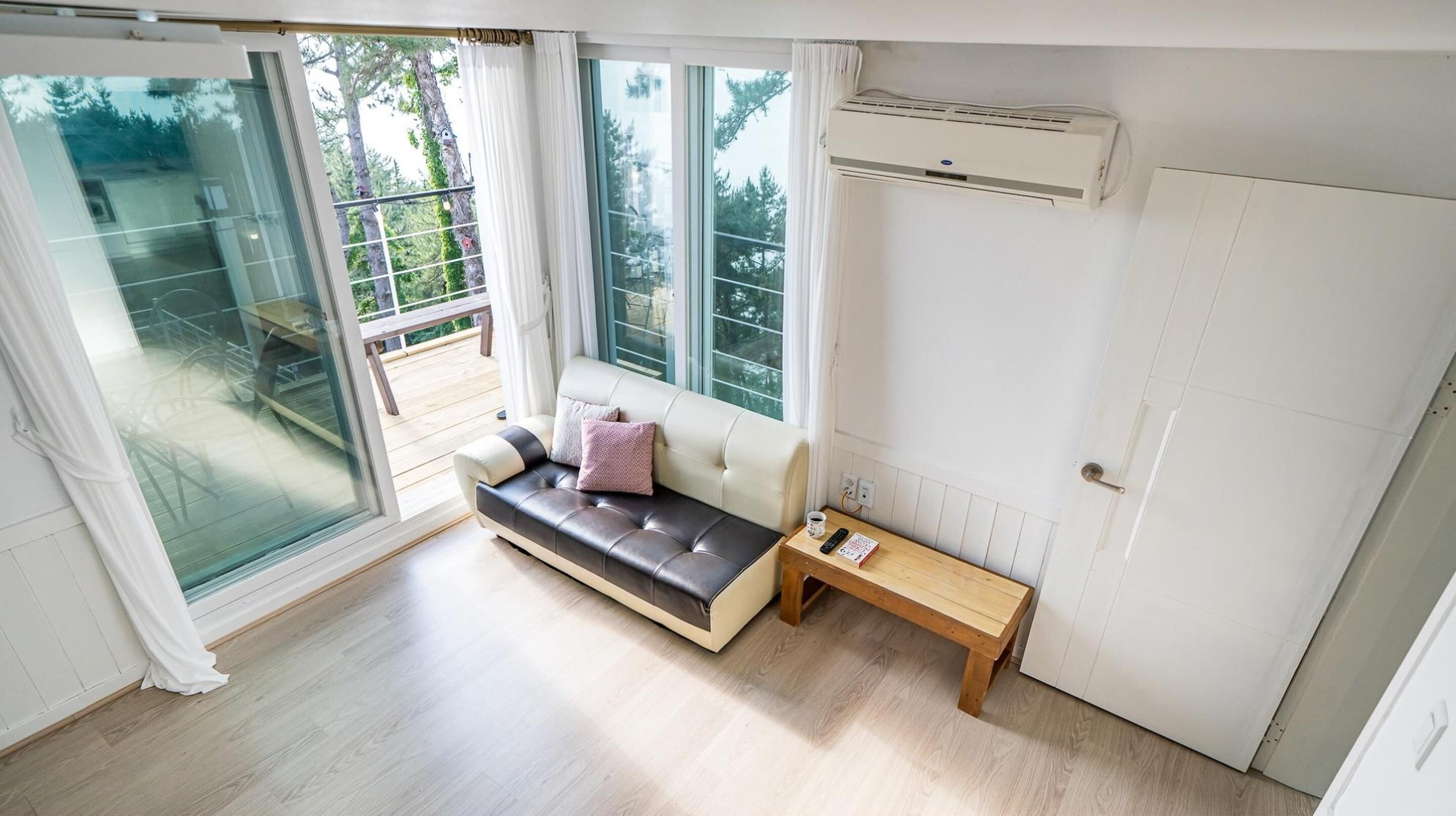 Quarto com sofá, uma mesa pequena e janela com cortinas.