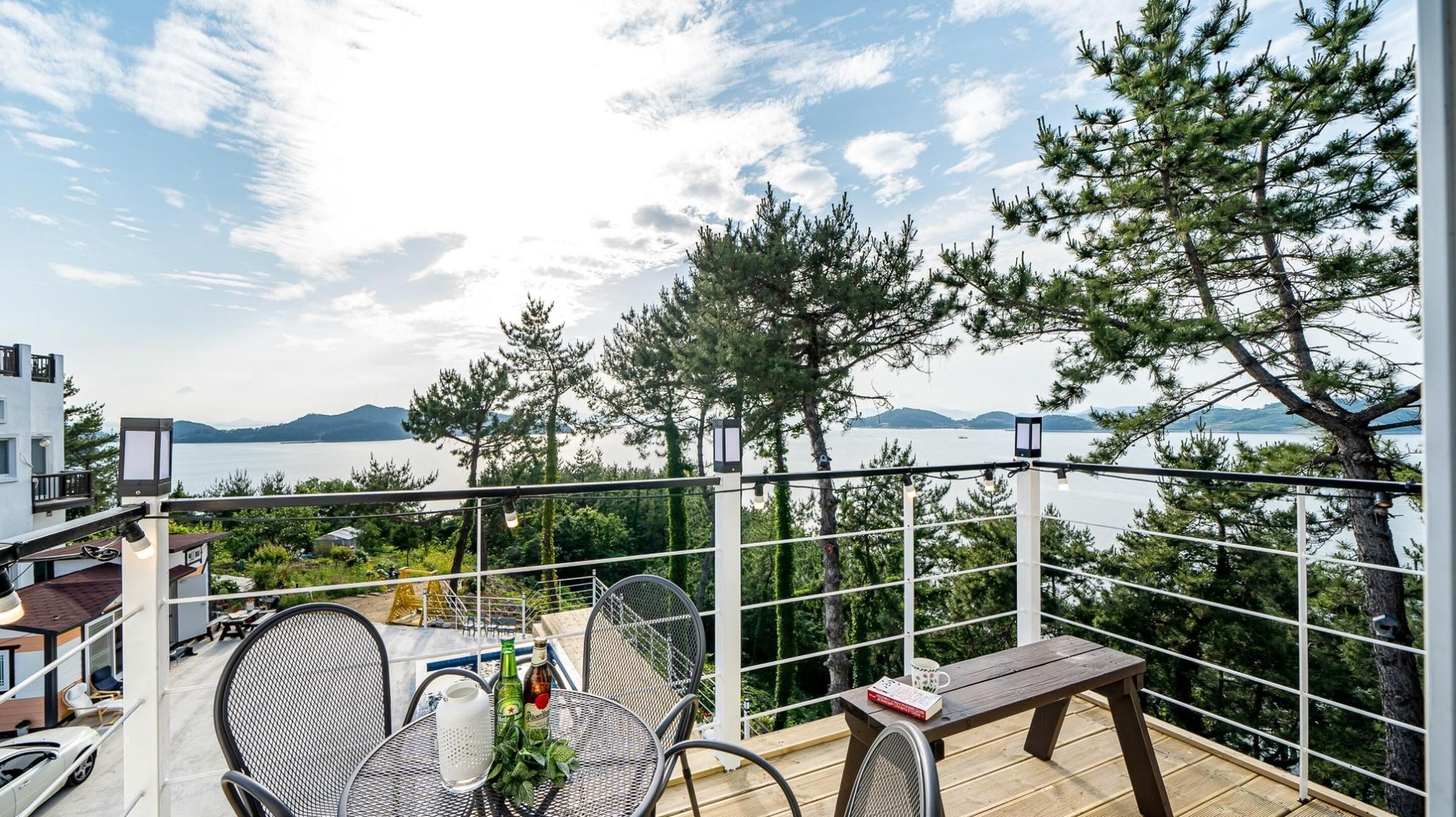 Varanda com área de estar externa, vista para um lago e paisagem montanhosa ao fundo.