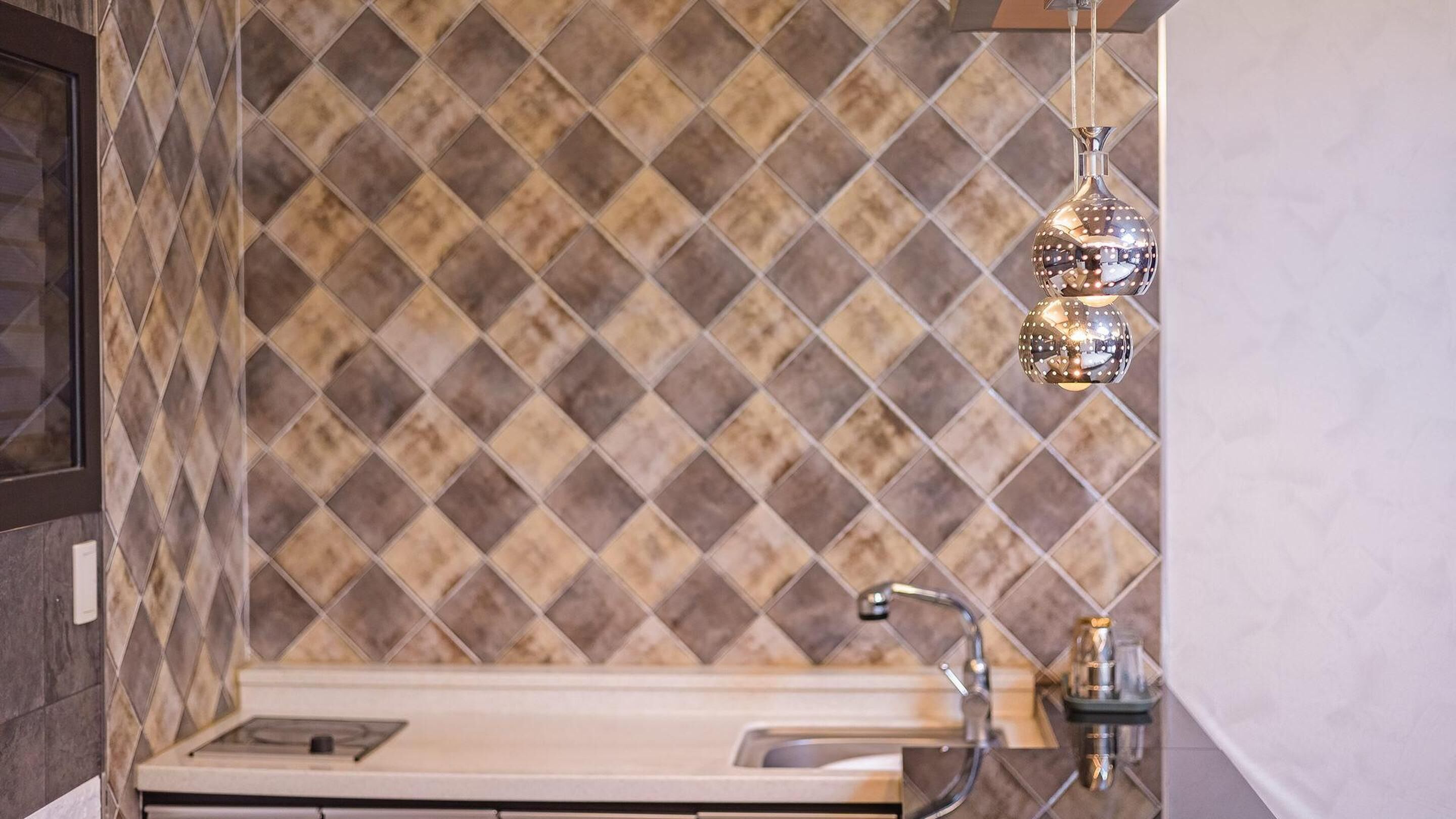 Uma cozinha com painel de fundo em padrão de losangos, uma pia de aço inoxidável e um lustre.