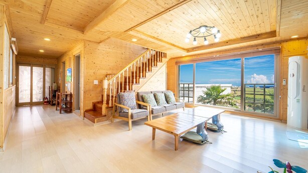 Uma sala de estar espaçosa com escada de madeira, um conjunto de sofás e uma grande janela com vista para o exterior.