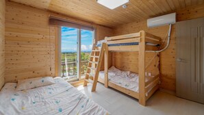 Quarto de cabana de madeira com beliches, escada, janela com vista e ar condicionado.