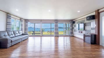 Uma sala de estar espaçosa com uma grande janela com vista para o mar, um sofá de couro e uma televisão de tela plana na parede.