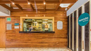 Uma área de recepção com parede de madeira, balcão de atendimento e placa com a inscrição 'ayenda hotels'.