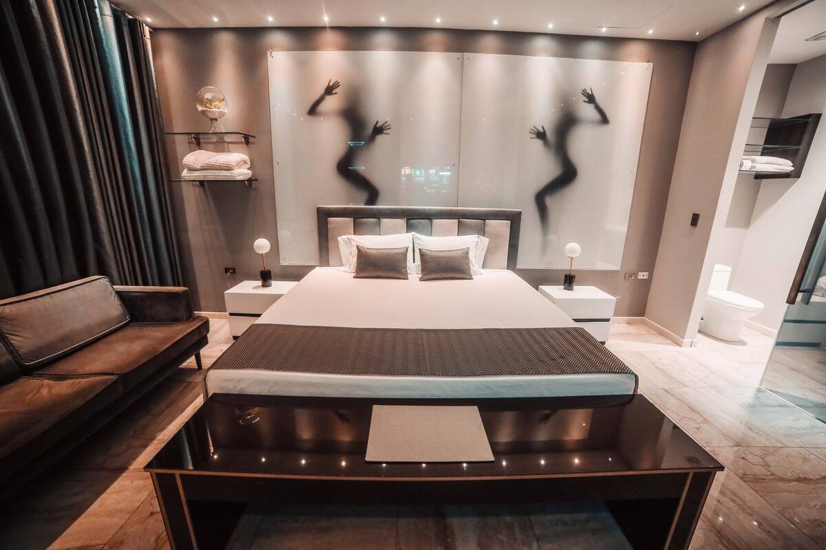 Quarto moderno com uma cama grande, um sofá de couro escuro e uma mesa de centro de vidro.
