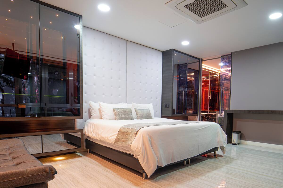 Quarto moderno com uma cama grande, parede de vidro e vista para a cidade.
