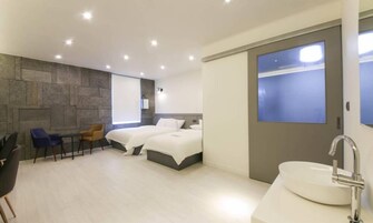 Quarto de hotel moderno com duas camas, um espelho grande, pia e um espaço de estar com cadeiras.