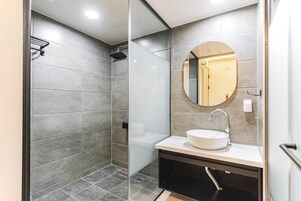 Uma casa de banho moderna com cabine de duche em vidro, espelho redondo e lavatório branco.