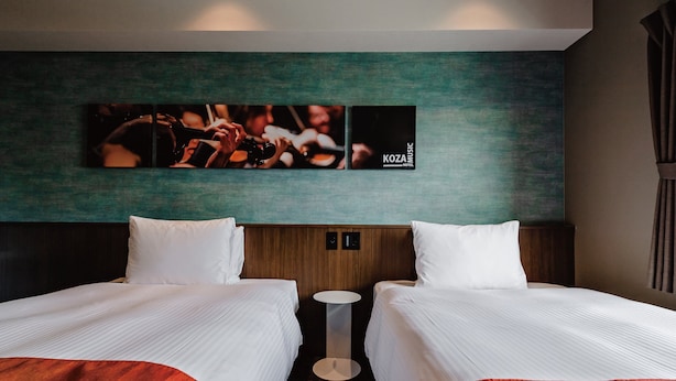 Quarto de hotel com duas camas, uma mesa redonda pequena e uma grande obra de arte na parede.