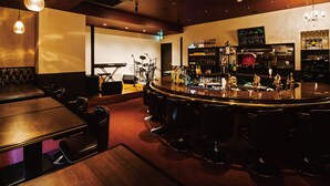 Um bar com palco, banquetas e diversos copos e garrafas no balcão.
