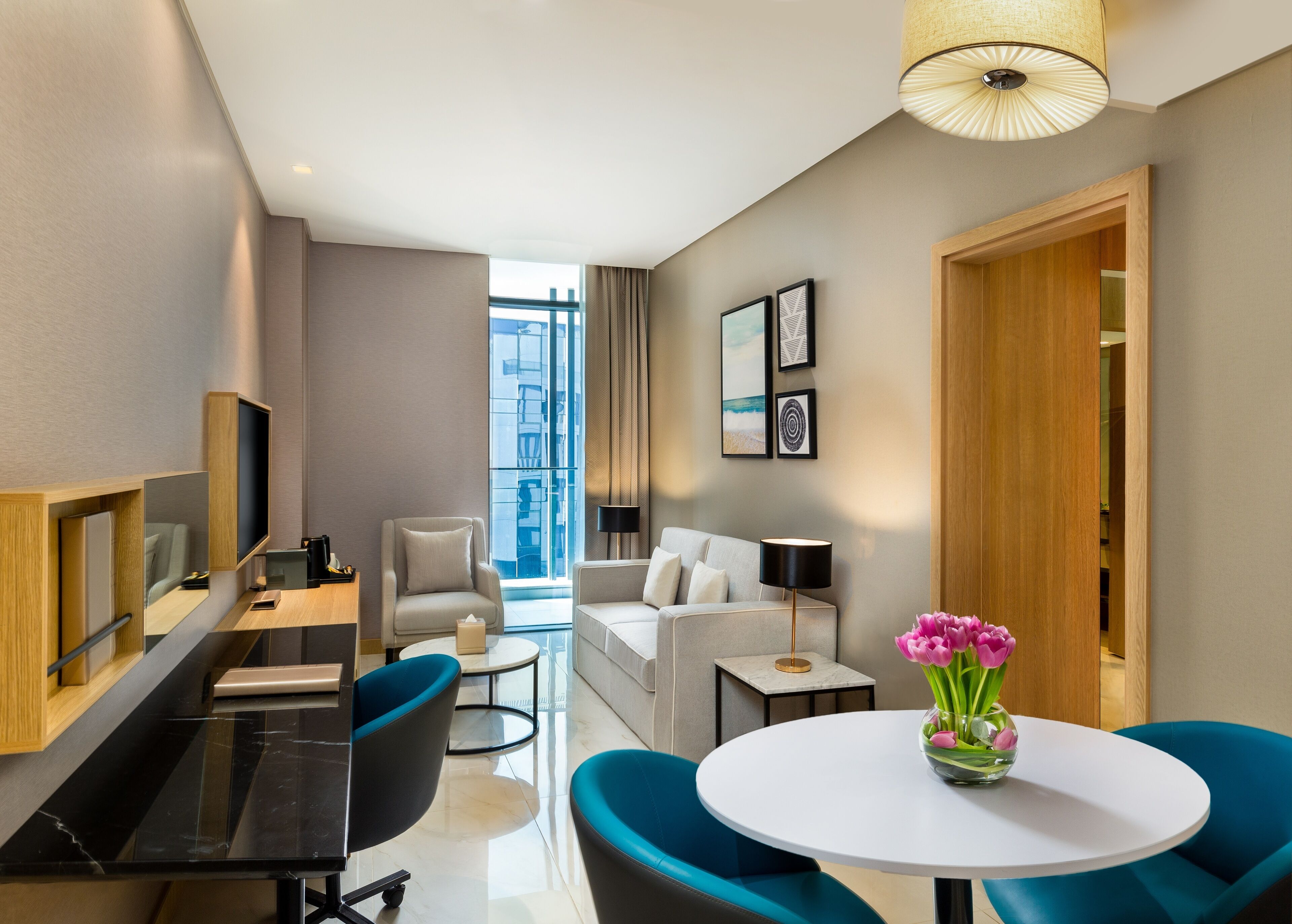 Quarto de hotel moderno com área de refeições, sofá, televisão e vista para a cidade.