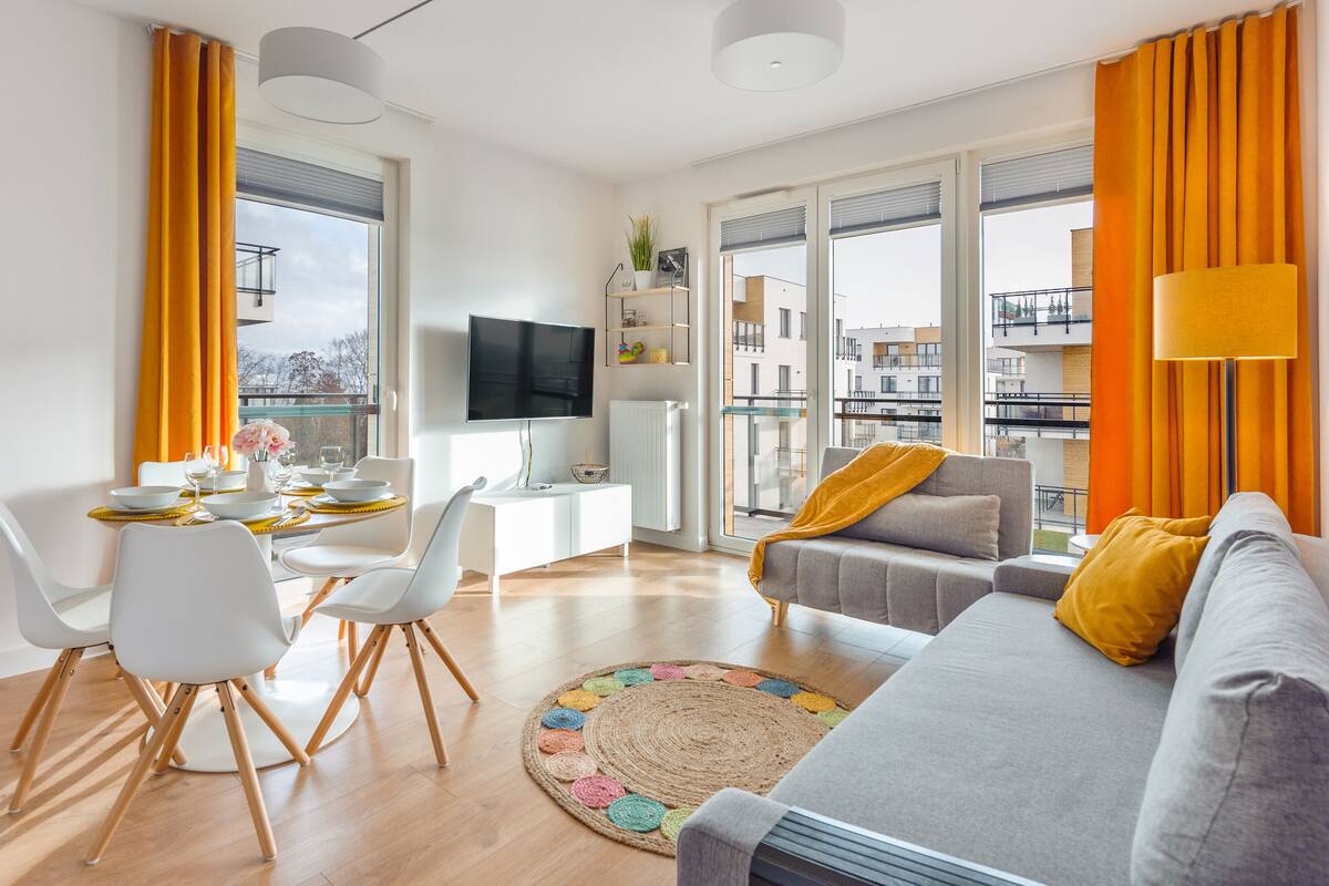 Uma sala de estar moderna com área de jantar, um sofá cinzento e uma televisão em um suporte branco.