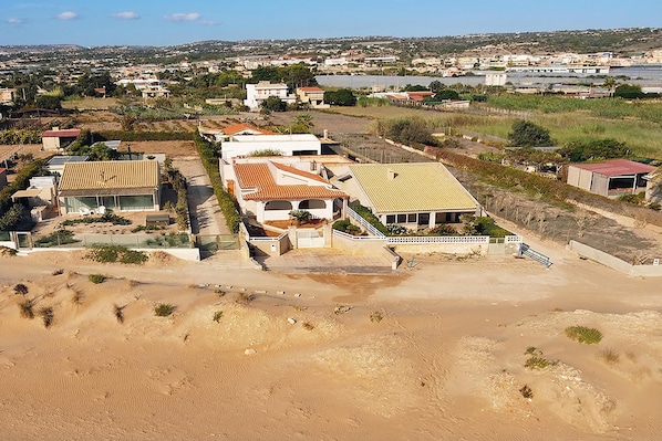 Área residencial com casas, um primeiro plano arenoso e um corpo d'água ao longe.