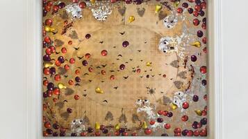 Obra de arte emoldurada com mapa antigo ao fundo, apresentando diversas frutas, pássaros e elementos decorativos.