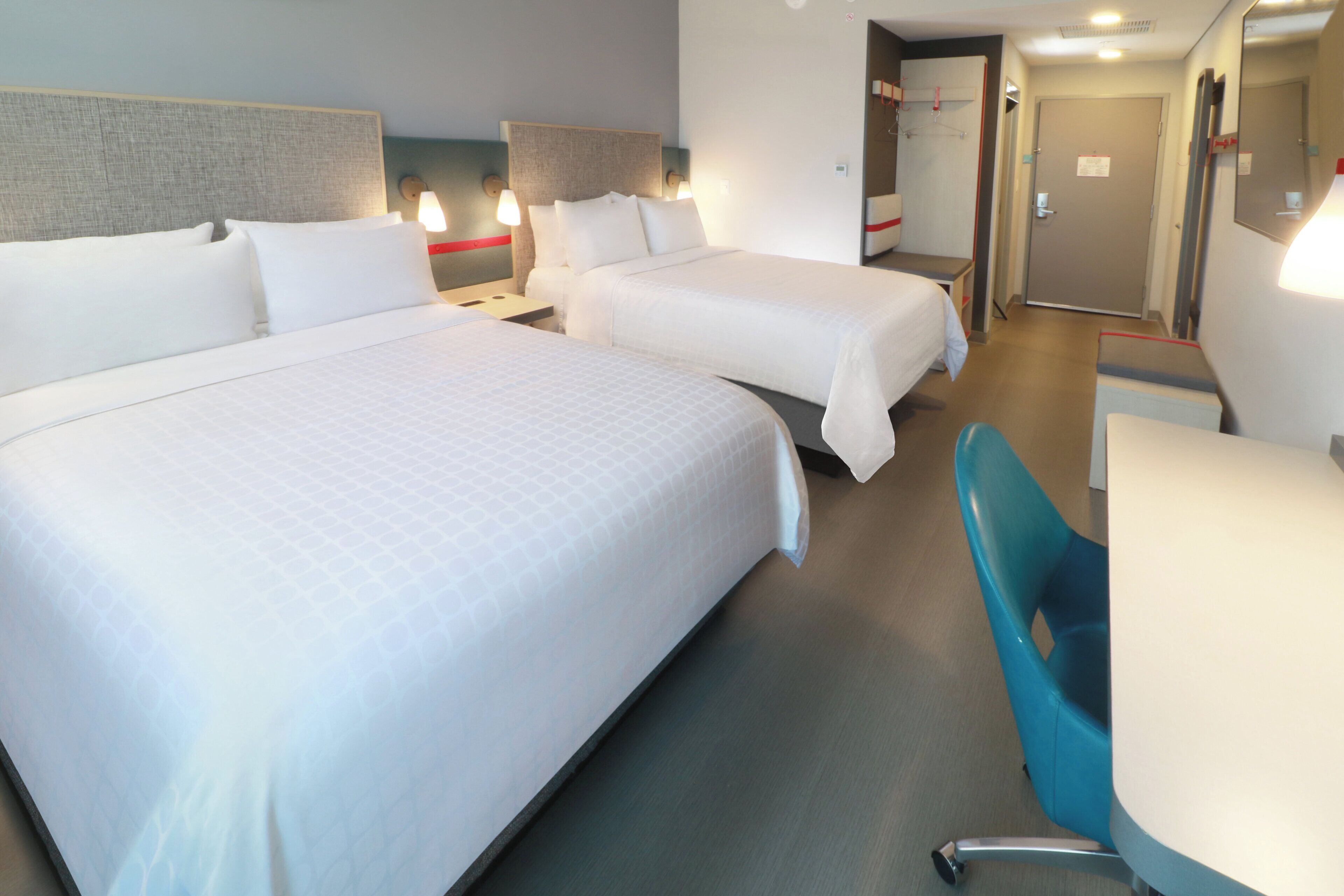 Quarto de hotel com duas camas, uma escrivaninha e uma cadeira.