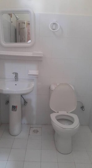 Casa de banho com lavatório, espelho, sanita e um pequeno caixote do lixo.