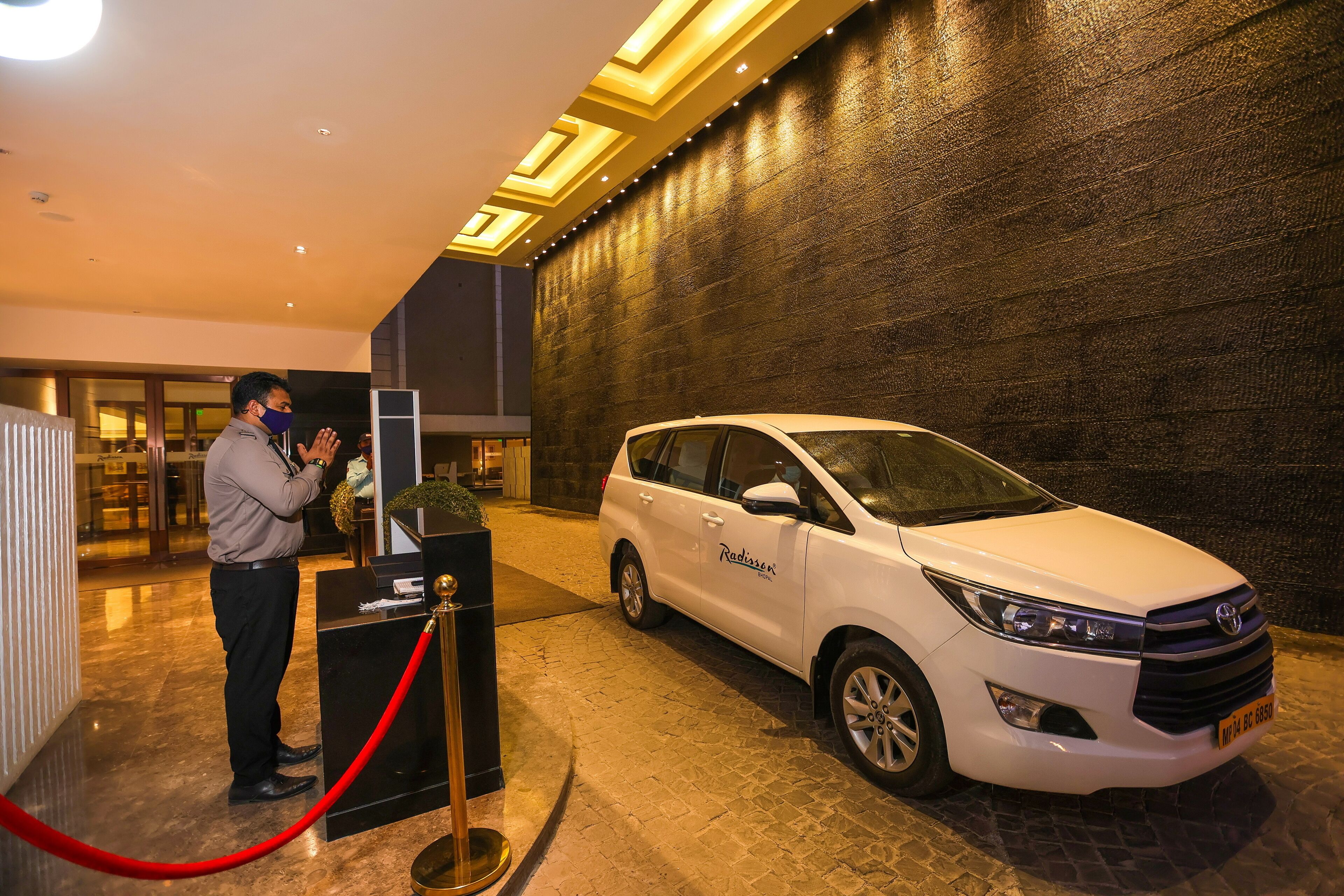 Um carro branco estacionado numa área interna bem iluminada, com um balcão de recepção e uma pessoa próxima.