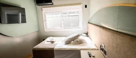 Quarto de hotel pequeno com uma cama, mesas de cabeceira, uma janela e uma kitchenette.