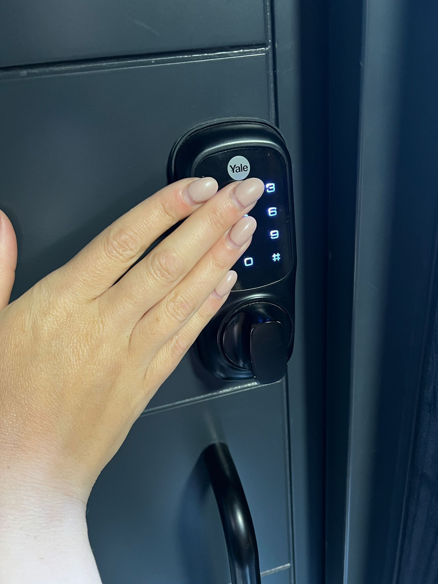 Uma mão usando uma fechadura eletrônica Yale em uma porta.