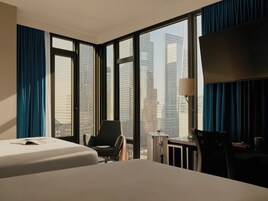 Quarto de hotel com uma cama grande, uma cadeira, uma mesa e vista para edifícios altos.