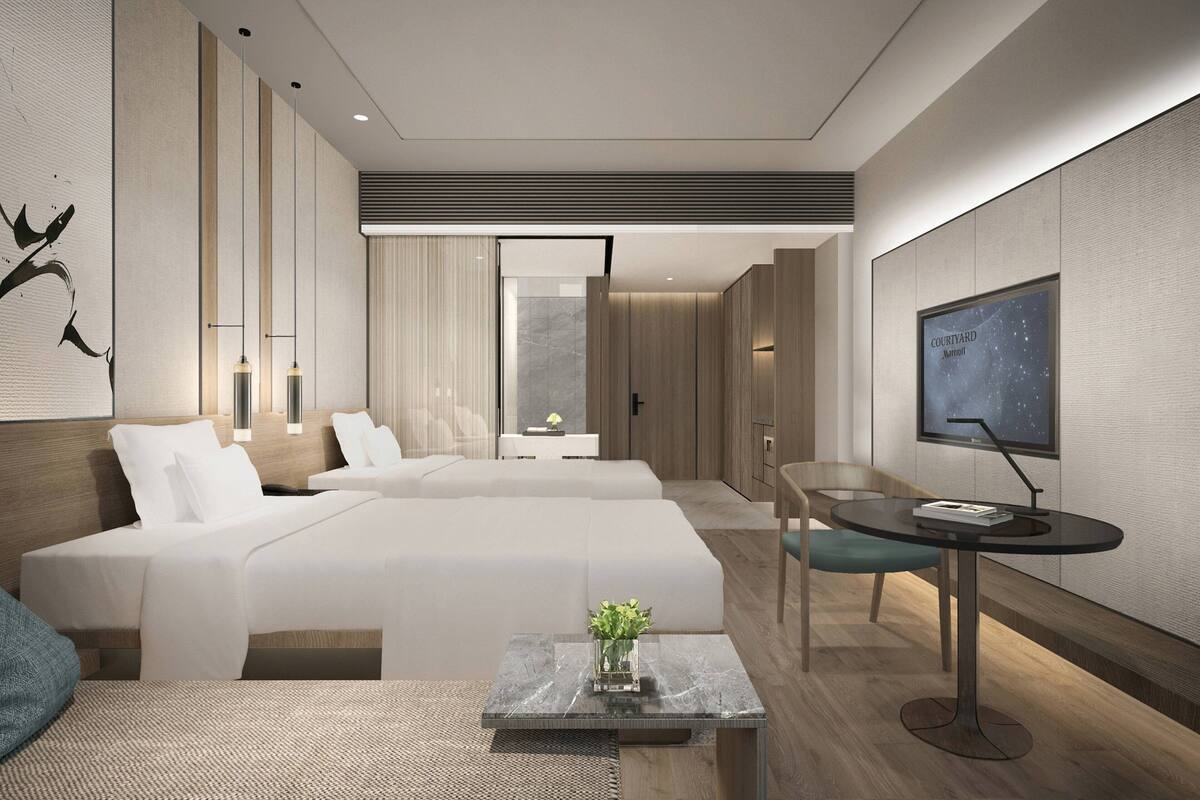 Quarto de hotel moderno com uma cama grande, uma escrivaninha com cadeira, televisão e vista para o pátio.