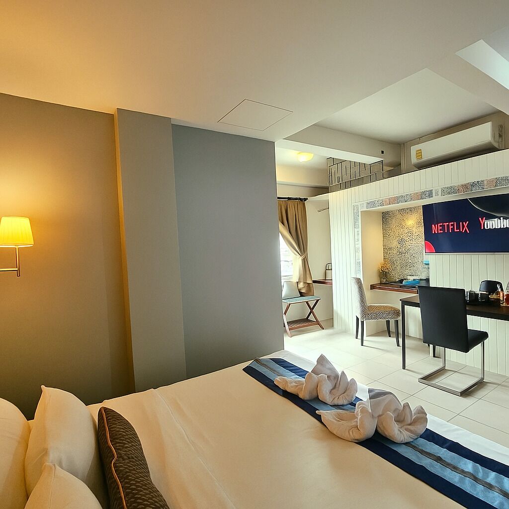 Quarto de hotel com cama, escrivaninha, cadeira e TV na parede exibindo o logotipo da Netflix.
