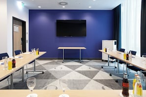 Uma sala de conferência com uma mesa grande, cadeiras, uma TV de tela plana e um quadro branco.