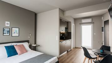 Quarto de hotel moderno com cama, mesa de cabeceira e área de kitchenette.