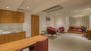 Uma sala de estar moderna com um sofá de madeira, duas poltronas vermelhas, uma mesa de jantar e uma área de cozinha com pia e bancada.