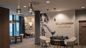 Um lobby moderno com uma placa 'WELCOME', um mural de bicicleta grande e uma área de estar com uma mesa redonda e cadeiras.