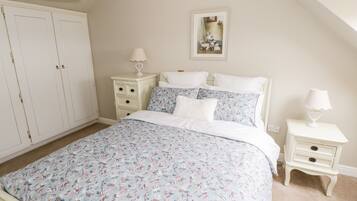 Quarto com cama, mesas de cabeceira brancas, um guarda-roupa branco e luminária no teto.