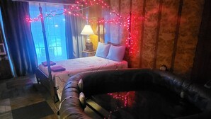 Um quarto acolhedor com uma cama, um puff preto, uma luminária e luzes de cordão.