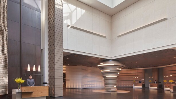Um lobby moderno com balcão de recepção, vários postos de atendimento e um imponente pilar decorativo central.