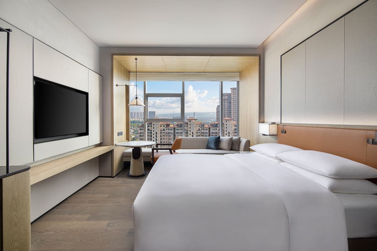 Quarto de hotel com cama grande, televisão, sofá, mesa de jantar e vista para a cidade.