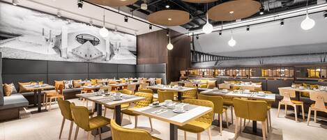 Uma sala de jantar moderna com várias mesas e cadeiras, apresentando um mural grande na parede e luminárias pendentes.