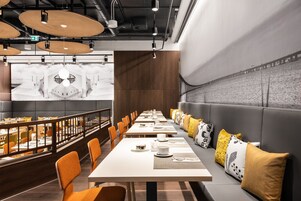 Um restaurante com mesas compridas, cadeiras laranja e um teto alto com luminárias pendentes.