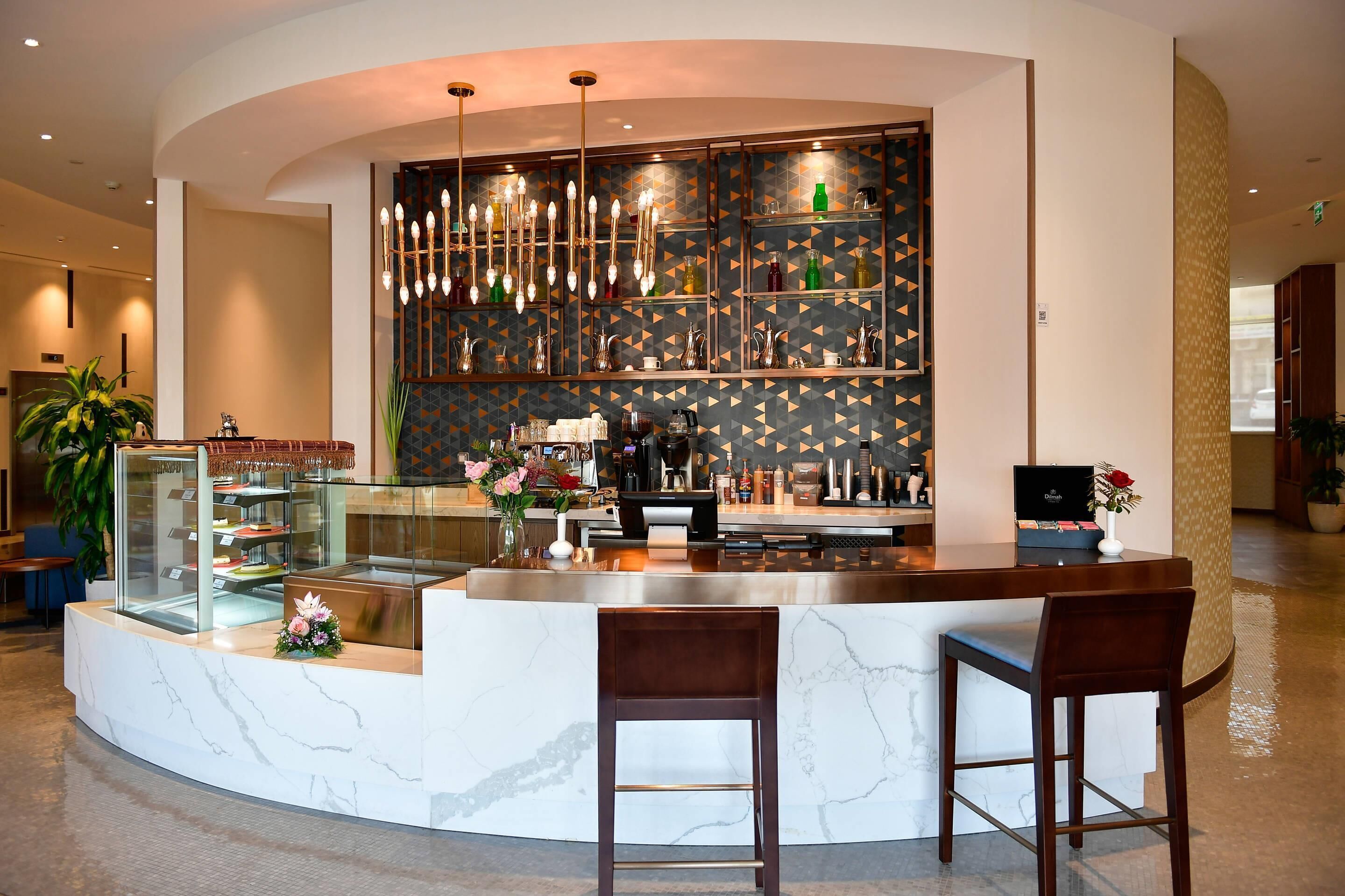 Uma área de bar moderna com balcão de mármore curvo, dois banquetas e uma parede decorativa com prateleiras.