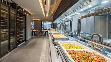 Uma área de buffet com diversas opções de comida, um espaço de estar com mesas e cadeiras, e um design interior moderno com elementos de madeira no teto.