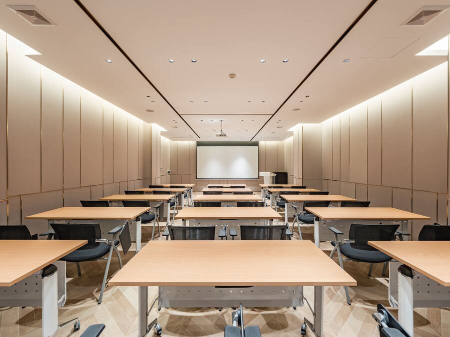 Uma sala de conferências com várias mesas e cadeiras, uma tela de projetor e iluminação embutida no teto.