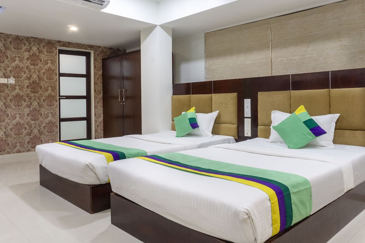 Quarto de hotel com duas camas, um guarda-roupa e um espelho grande.