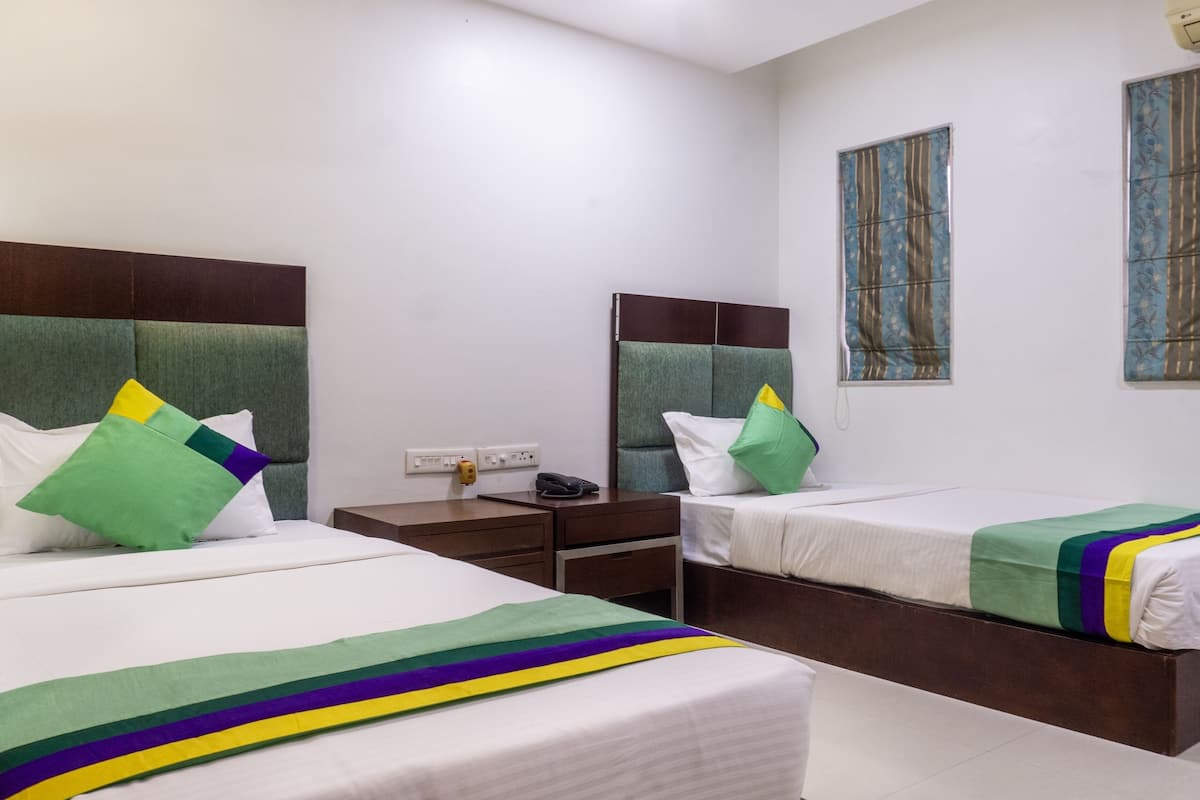 Quarto de hotel com duas camas de solteiro, mesa de cabeceira, espelho e janela com vista.