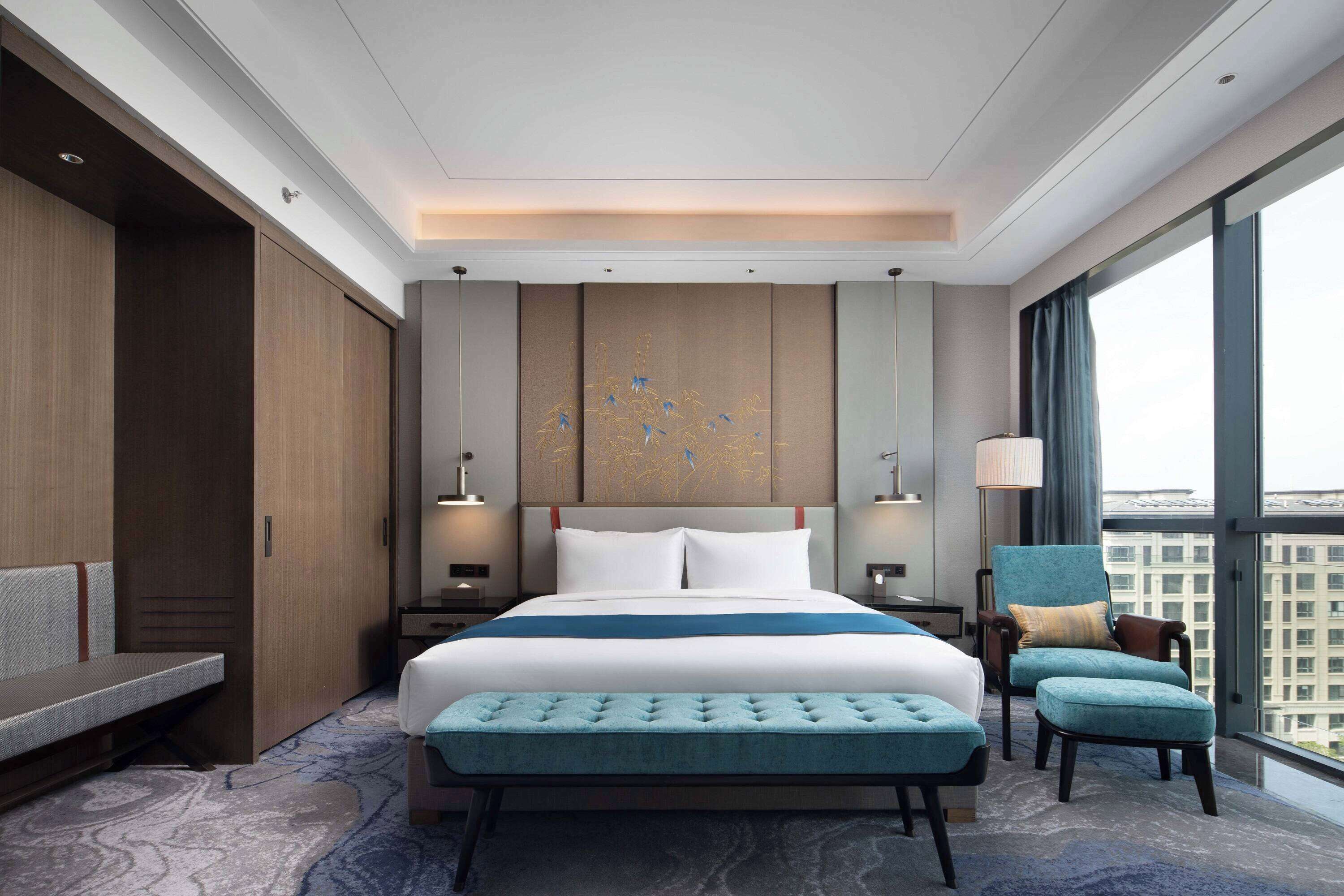 Quarto de hotel moderno com uma cama grande, área de estar, uma cadeira e vista para a cidade.