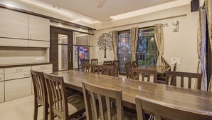 Uma sala de jantar com uma mesa de madeira comprida e cadeiras, um ventilador de teto e uma janela com cortinas.
