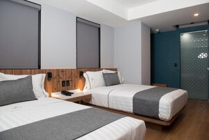 Quarto de hotel com duas camas, cabeceira de madeira, mesa de cabeceira com telefone e porta com padrão geométrico.