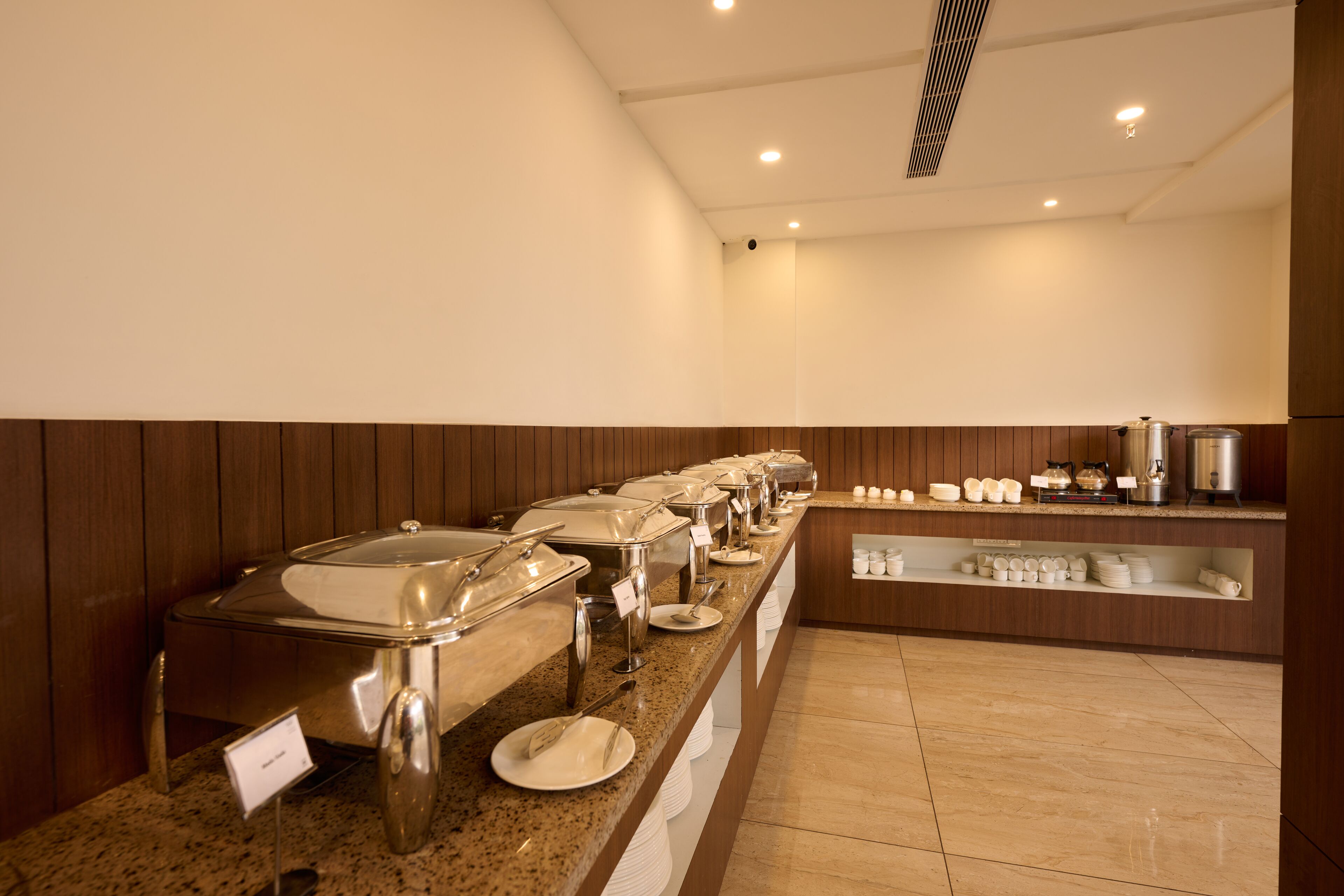 Buffet montado com diversas estações de serviço, balcão com pratos e prateleira com condimentos.