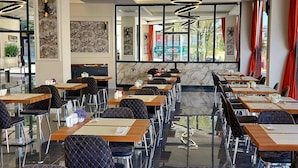 Um restaurante moderno com um amplo espaço de jantar, cadeiras estofadas em preto e mesas de madeira.