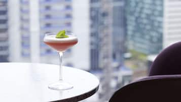 Um copo de martini com um ramo de hortelã sobre uma mesa redonda, com vista para um horizonte urbano ao fundo.
