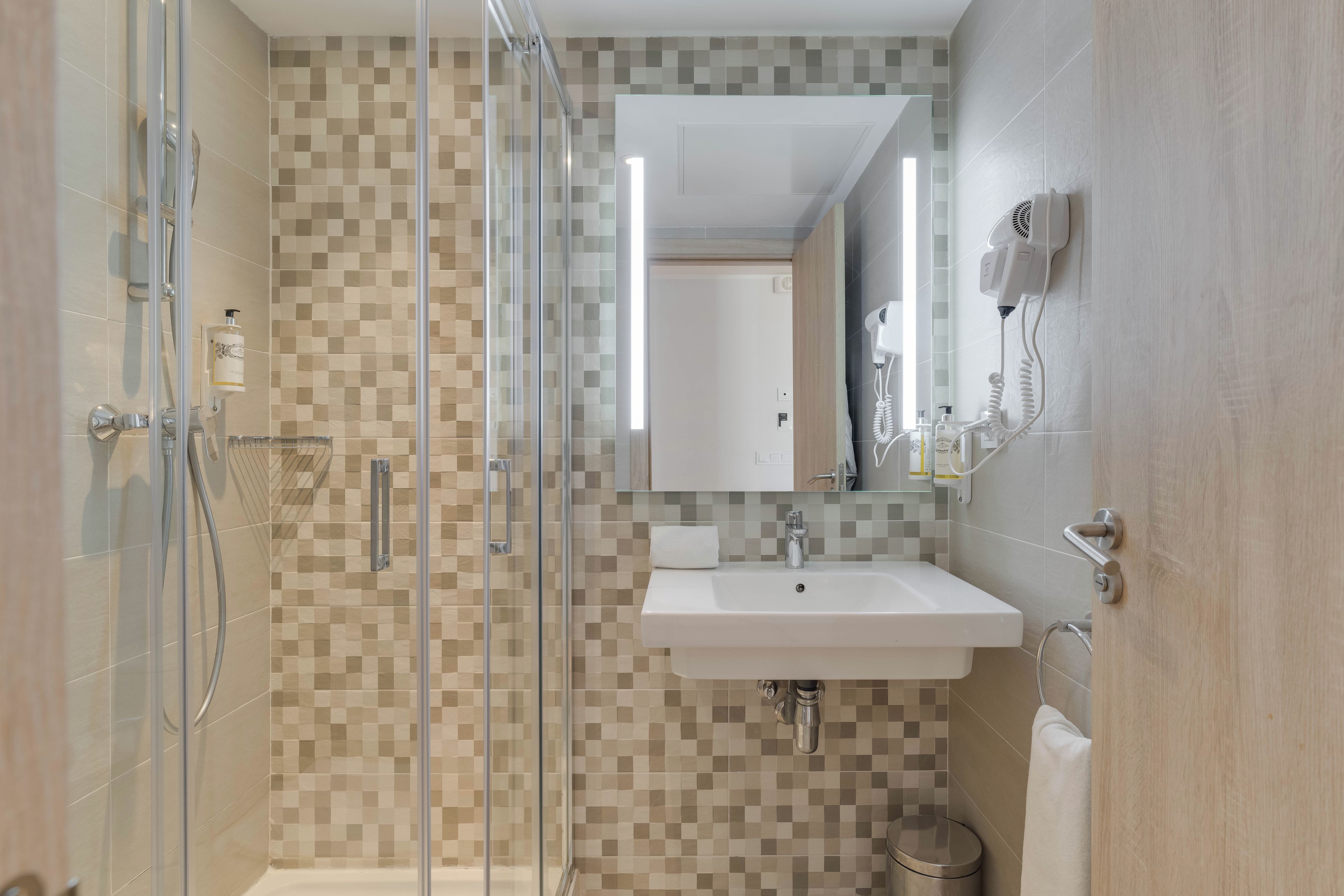 Casa de banho com cabine de duche em vidro, lavatório com espelho e secador de cabelo fixado na parede.