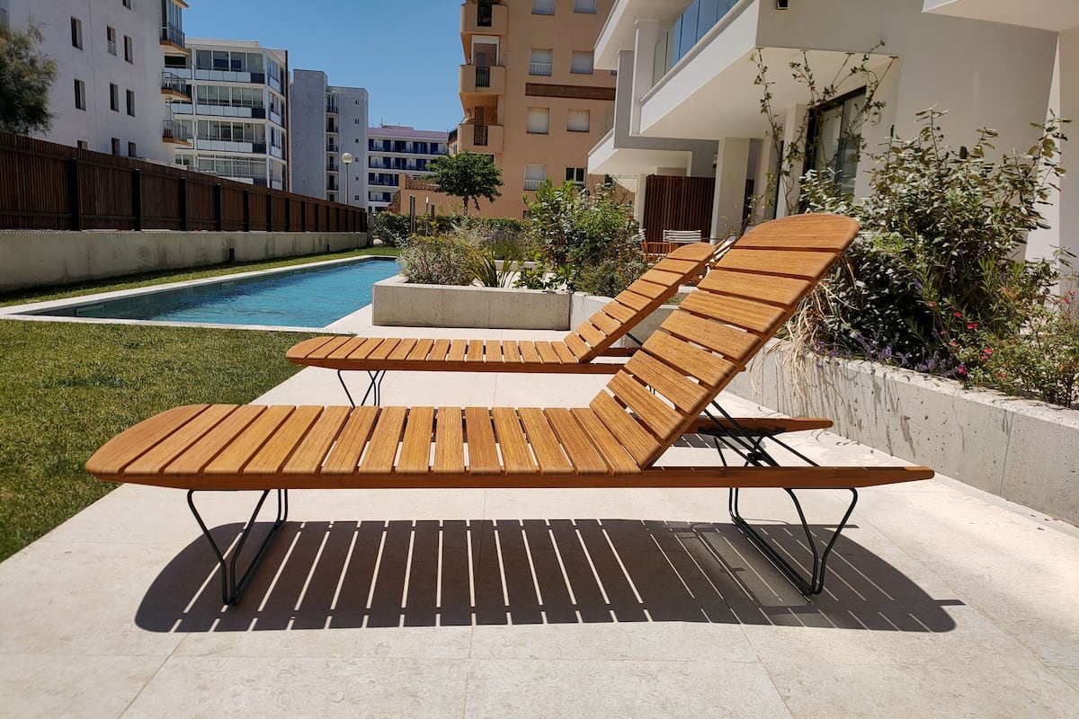 Uma área à beira da piscina com espreguiçadeiras de madeira e um deck de concreto.